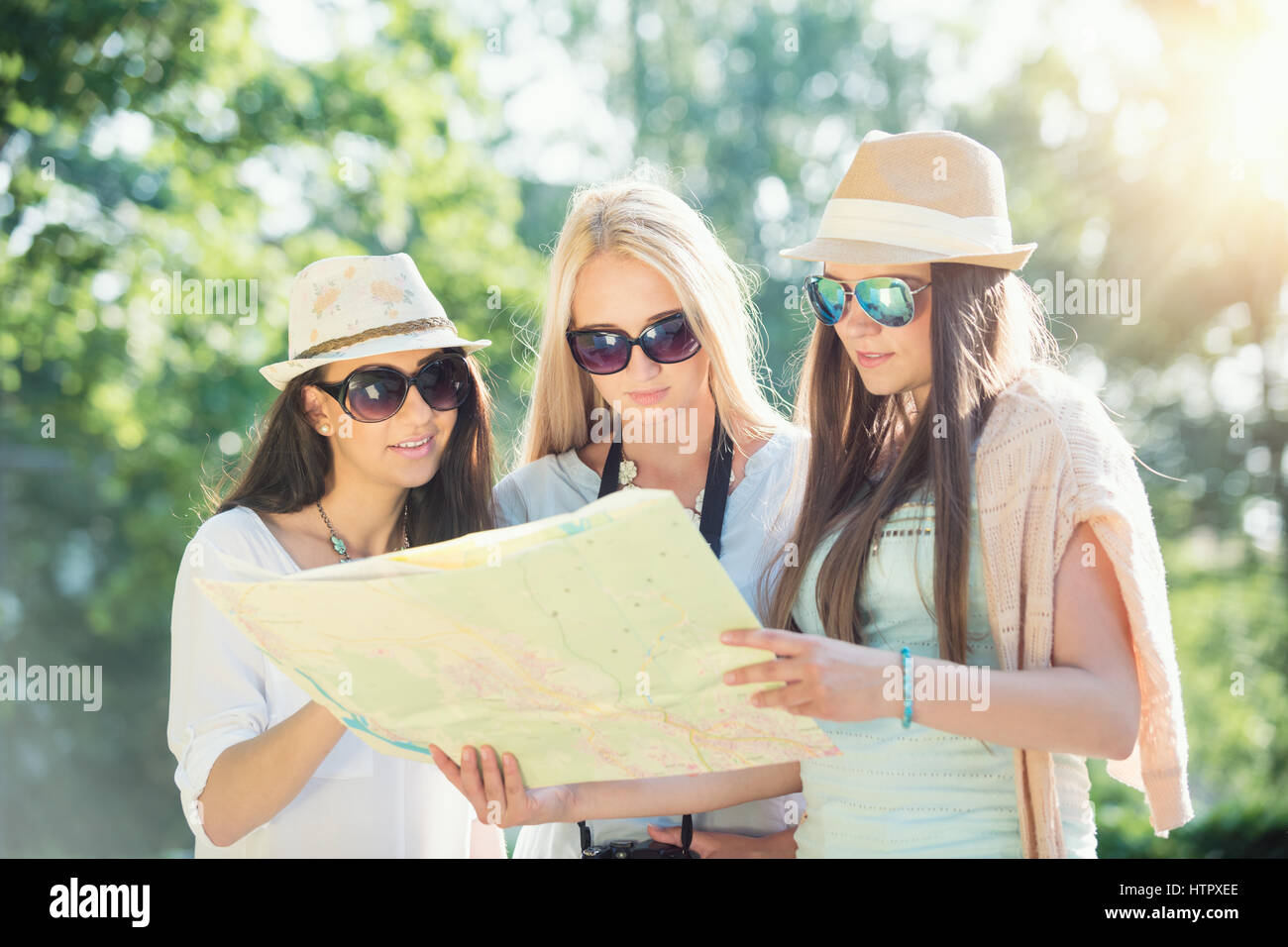 Three attractive girls looking for directions on a map at summer ...