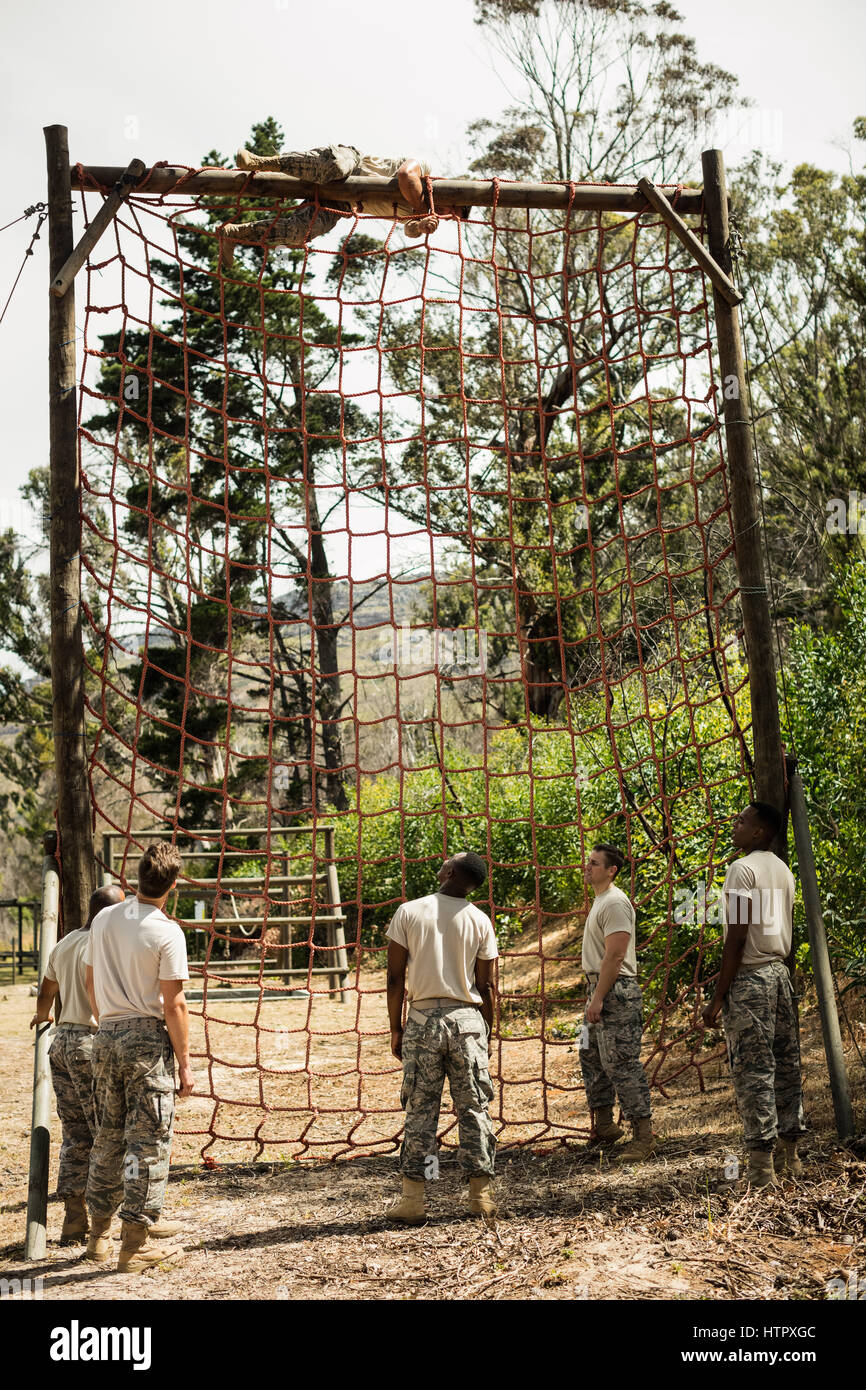 Military soldier climbing rope during obstacle course in boot camp ...