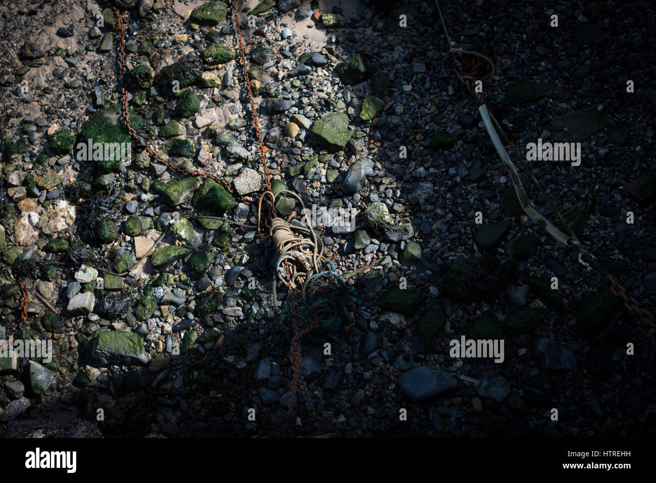 A rusty chain, ropes and exposed rocks and pebbles on the beach during ...