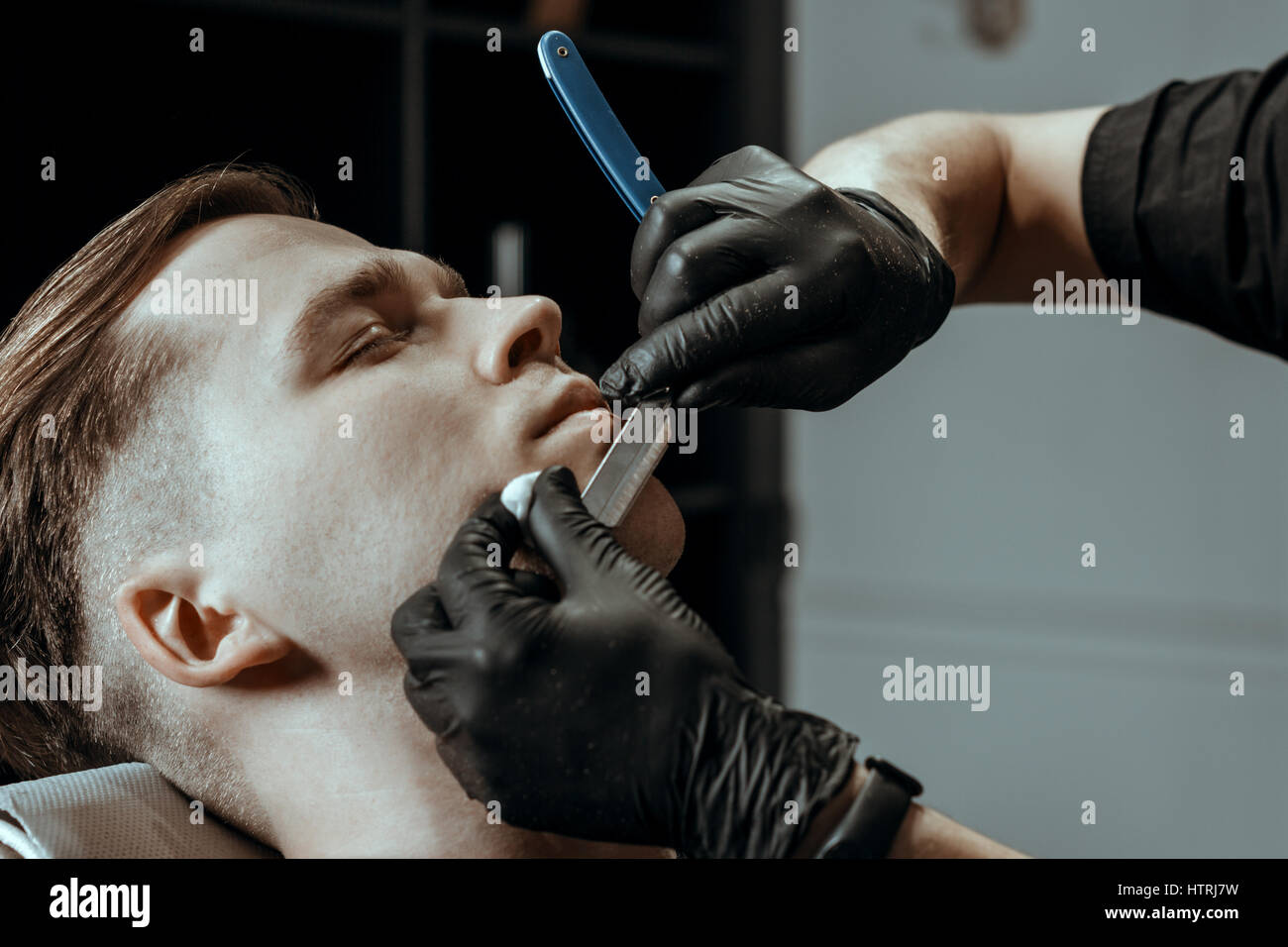 BARBERSHOP THEME. BARBER IN BLACK RUBBER GLOVES IS TRIMMING THE BEARD ...