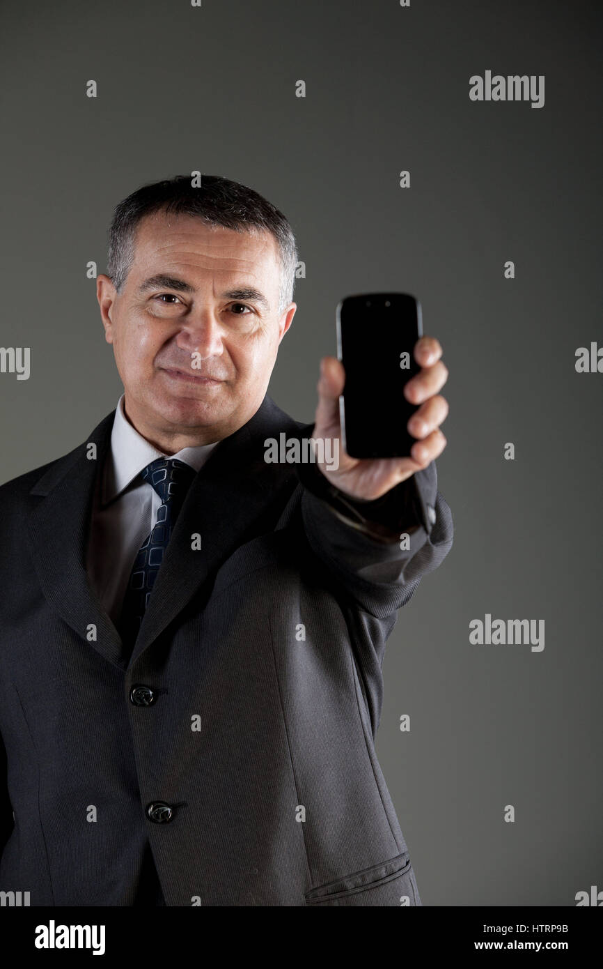 Serious businessman holding up a blank black smartphone towards the ...