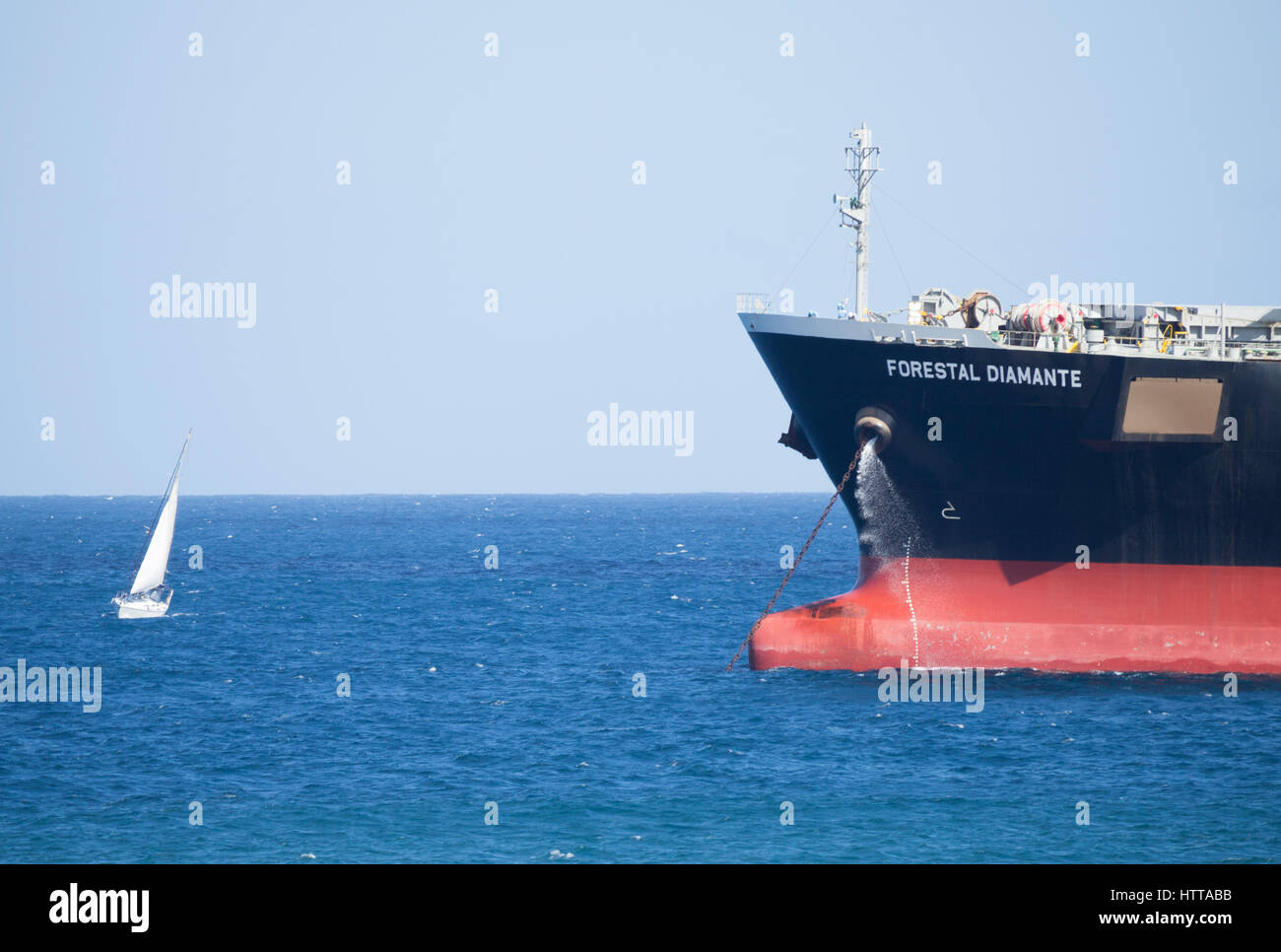 Small yacht sailing across bow of huge merchant ship Stock Photo - Alamy