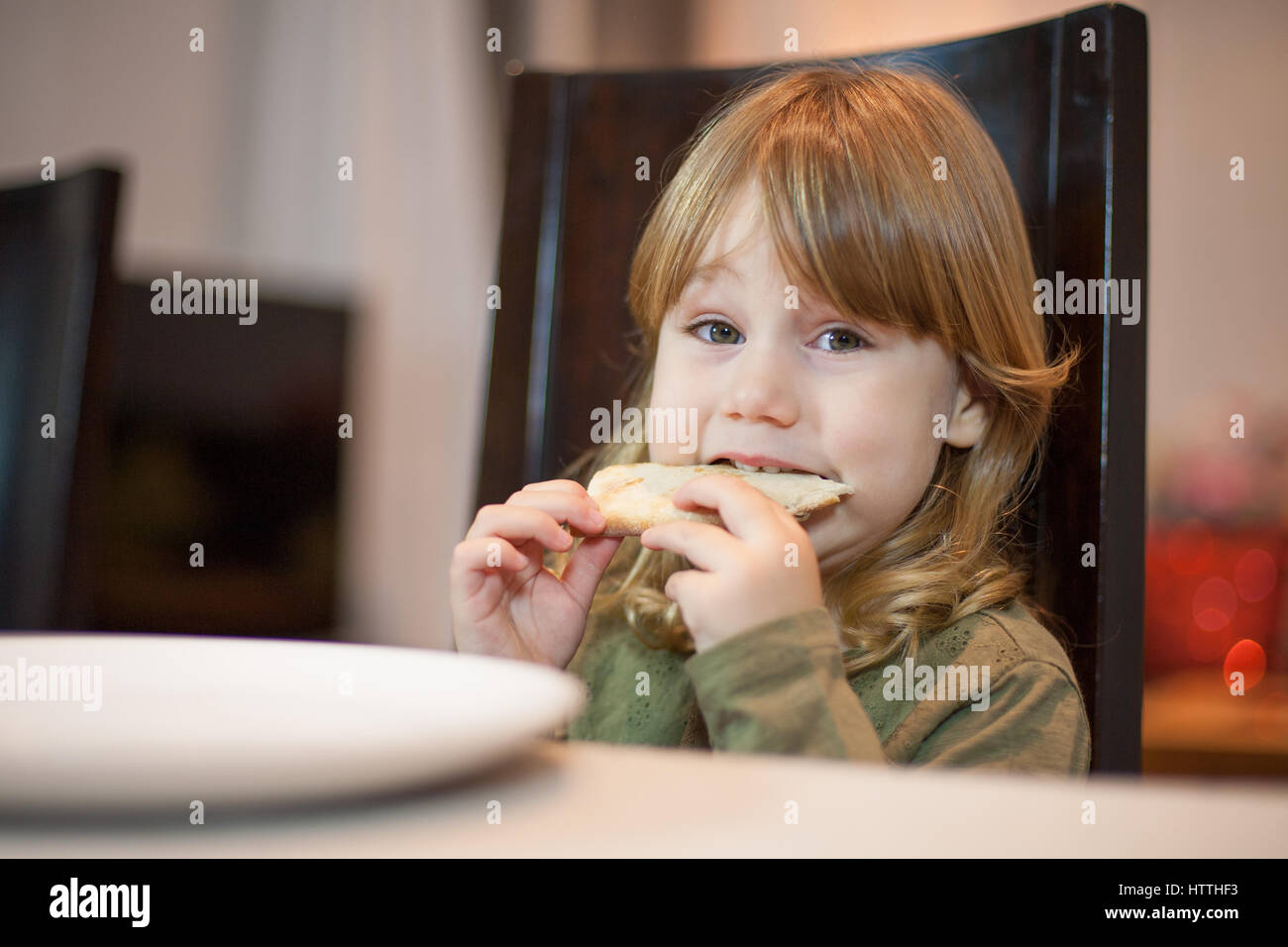 Three years old blonde hungry child biting pizza piece in her hands ...