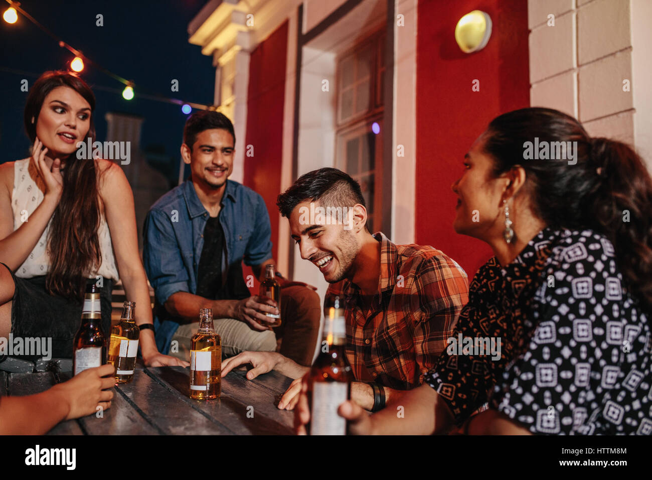Group of friends sitting around a table at rooftop party. Young people ...