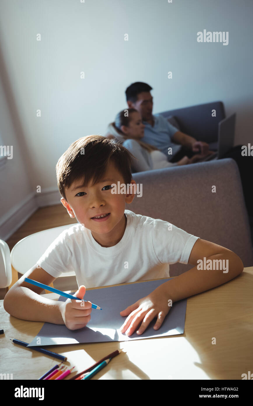 Portrait of happy boy drawing in paper while parents using laptop in ...