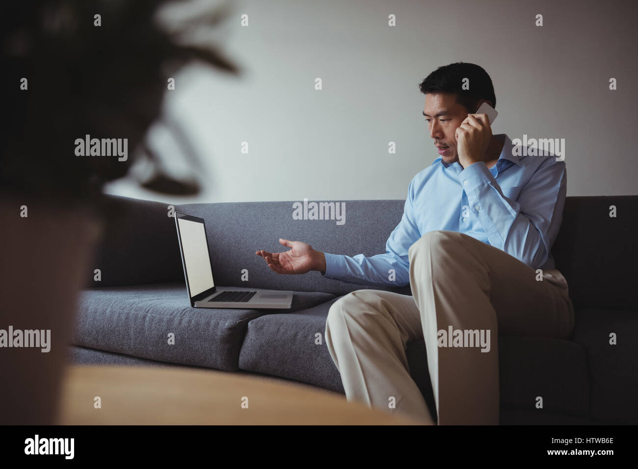 Man talking on mobile phone while using laptop in living room Stock ...