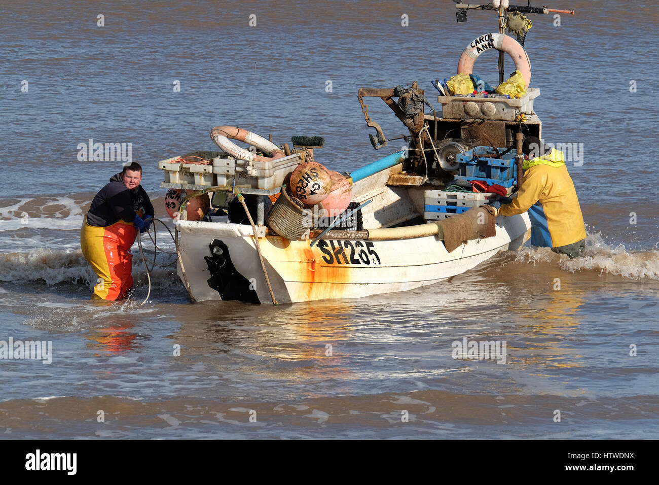 Small shell fishing boat with two man crew returning to beach at ...