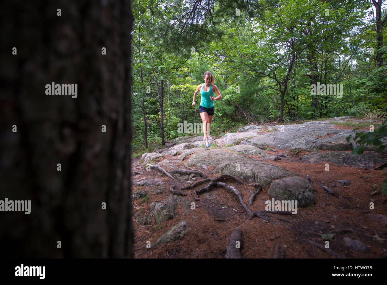 Young woman wearing fitness clothing running through forest on trail ...