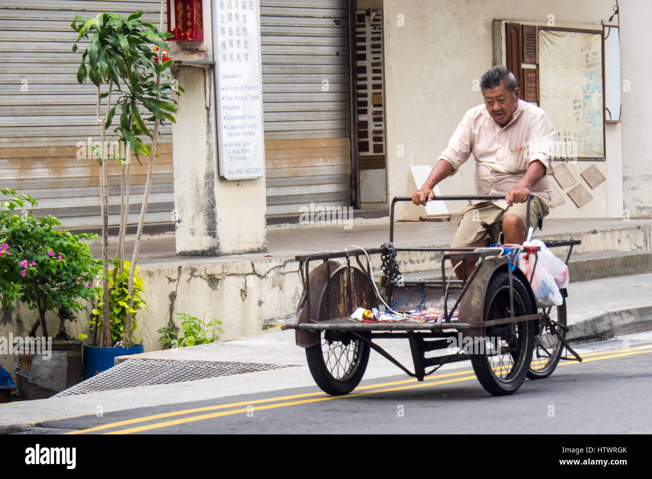 Singaporean man cycling a cargo tricycle used for transporting goods ...