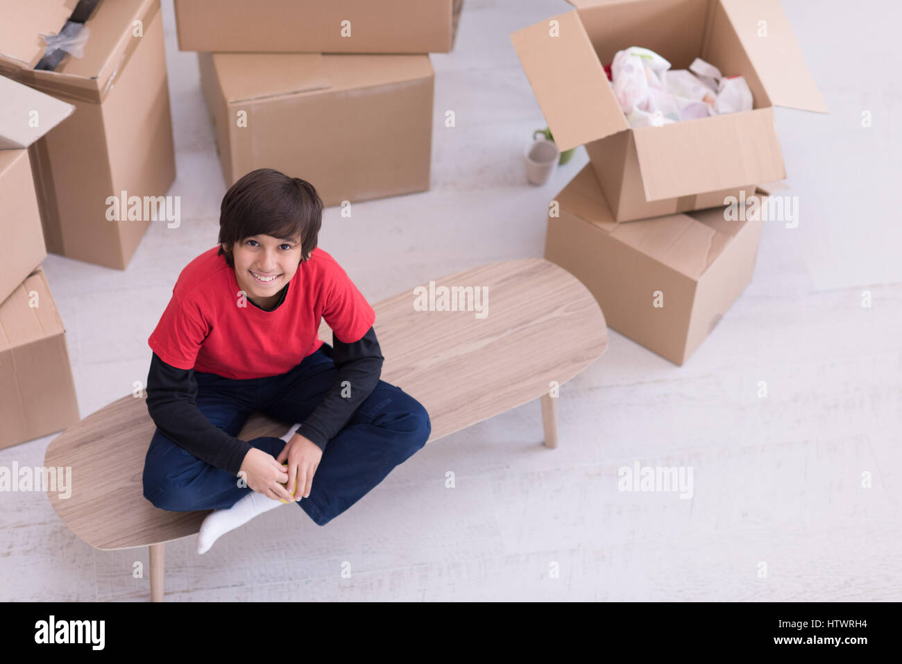 happy little boy sitting on the table with cardboard boxes around him ...