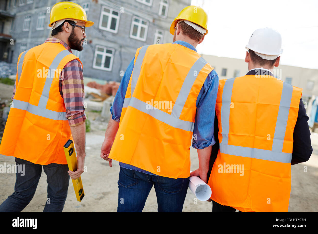 Rear view of three engineers moving towards construction-site and ...