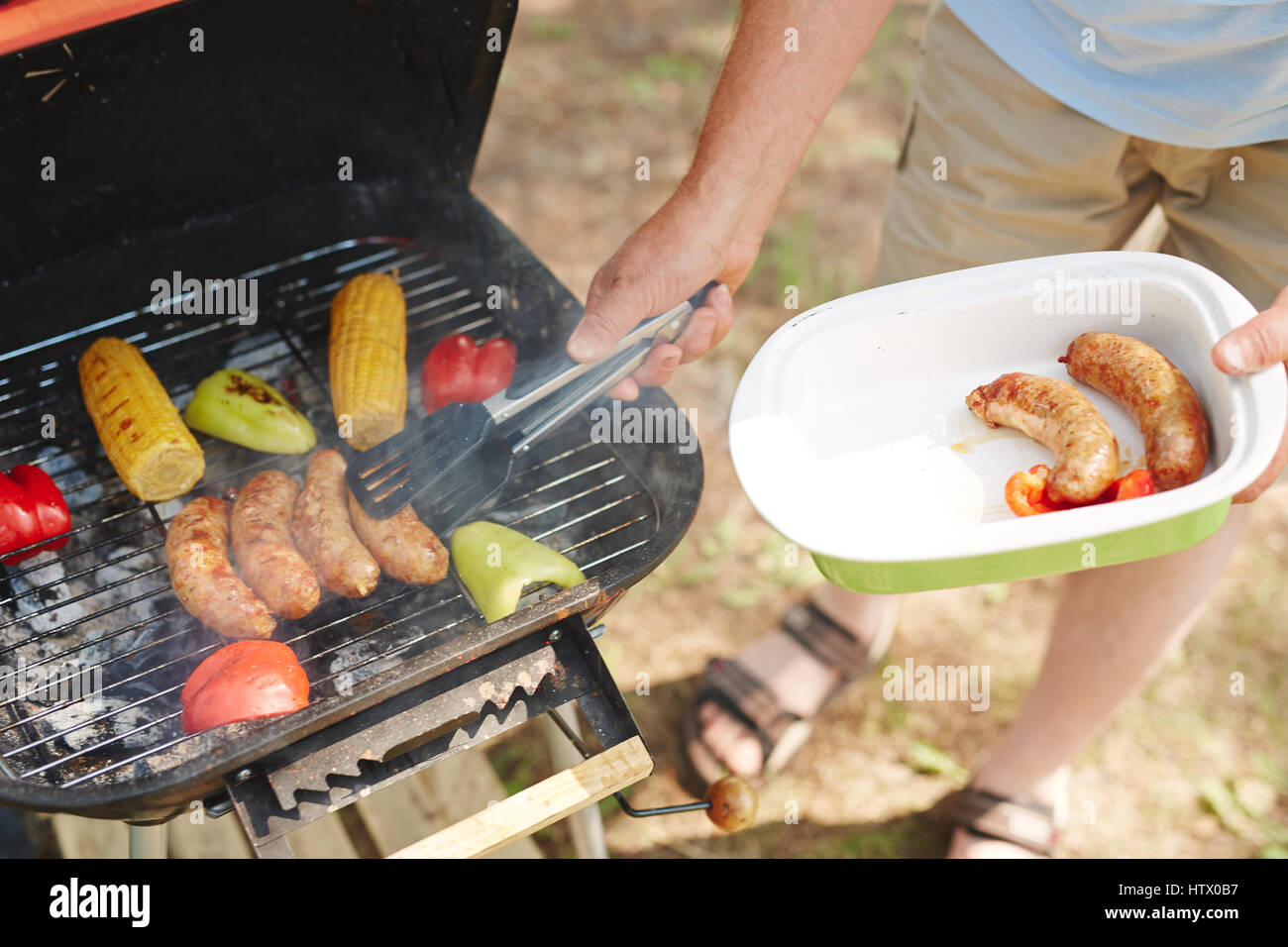 Human roasting sausages and vegetables and putting them into container ...