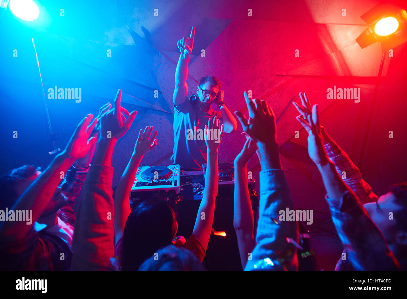Deejay in headphones raising his hand and enjoying disco with the crowd ...