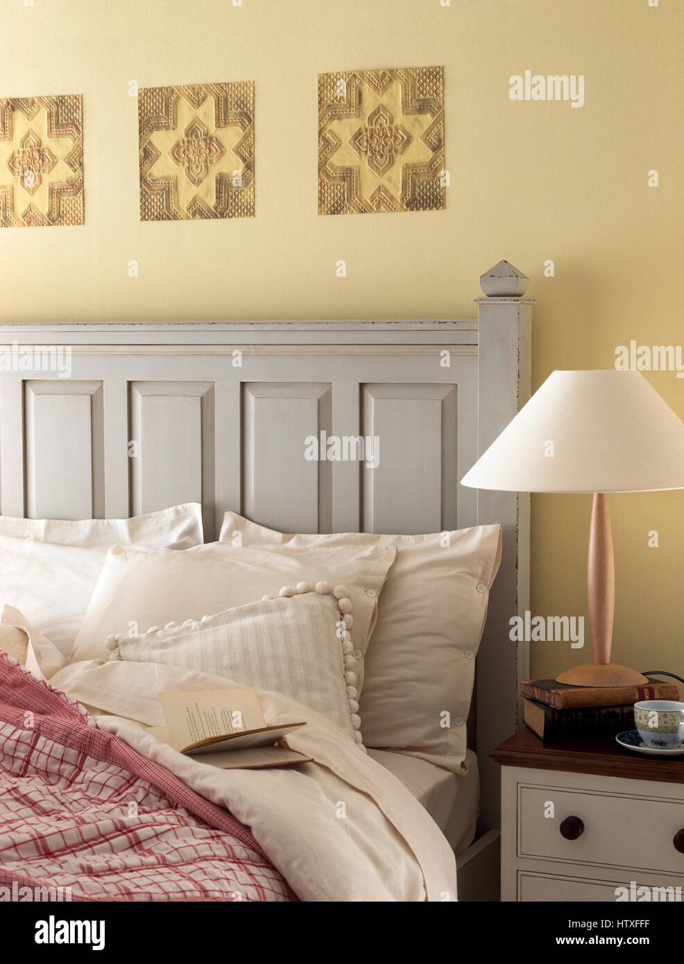 Decorative collage pictures on wall above a grey painted bed piled with ...