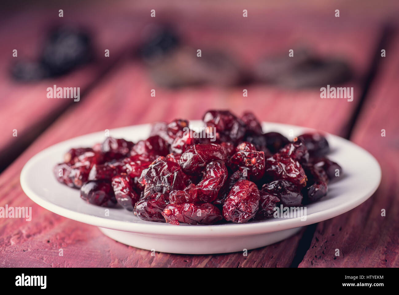 Dried cranberries on the white round plate on the red wooden surface ...