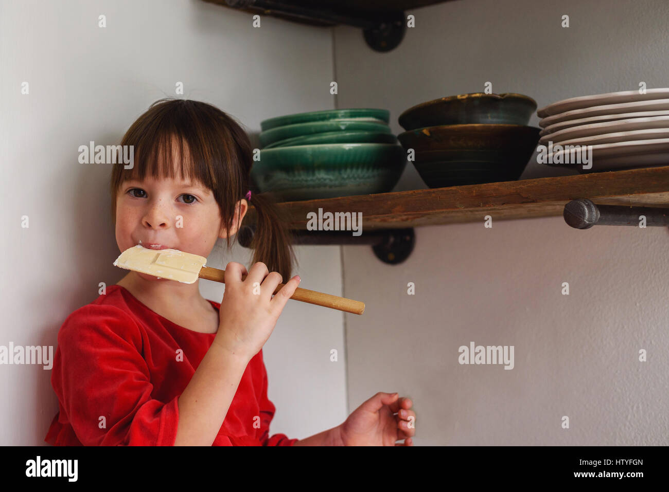 Girl sitting on kitchen counter with a spatula eating frosting Stock ...
