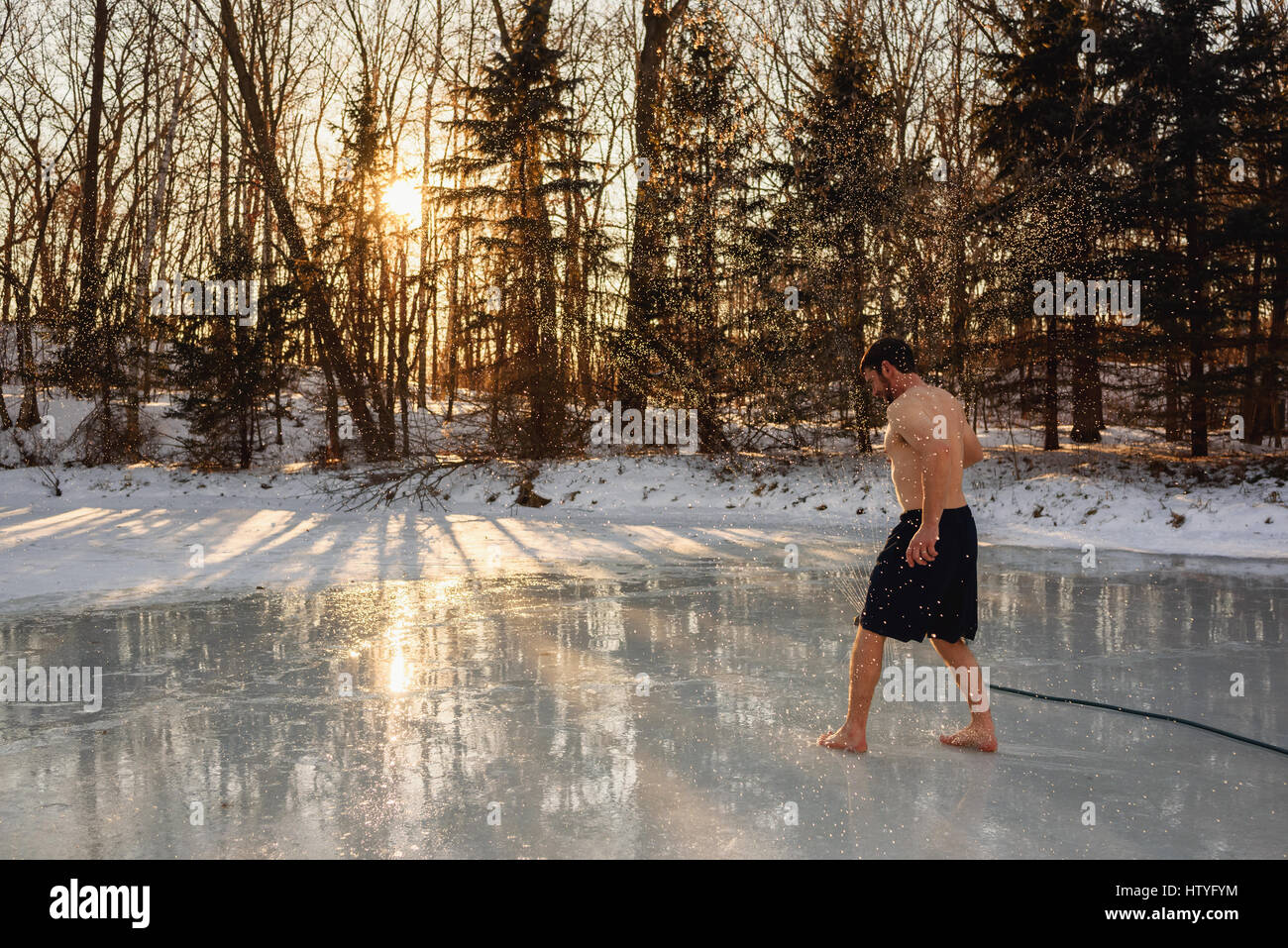 Man in swimming trunks running through sprinkler on frozen lake Stock ...