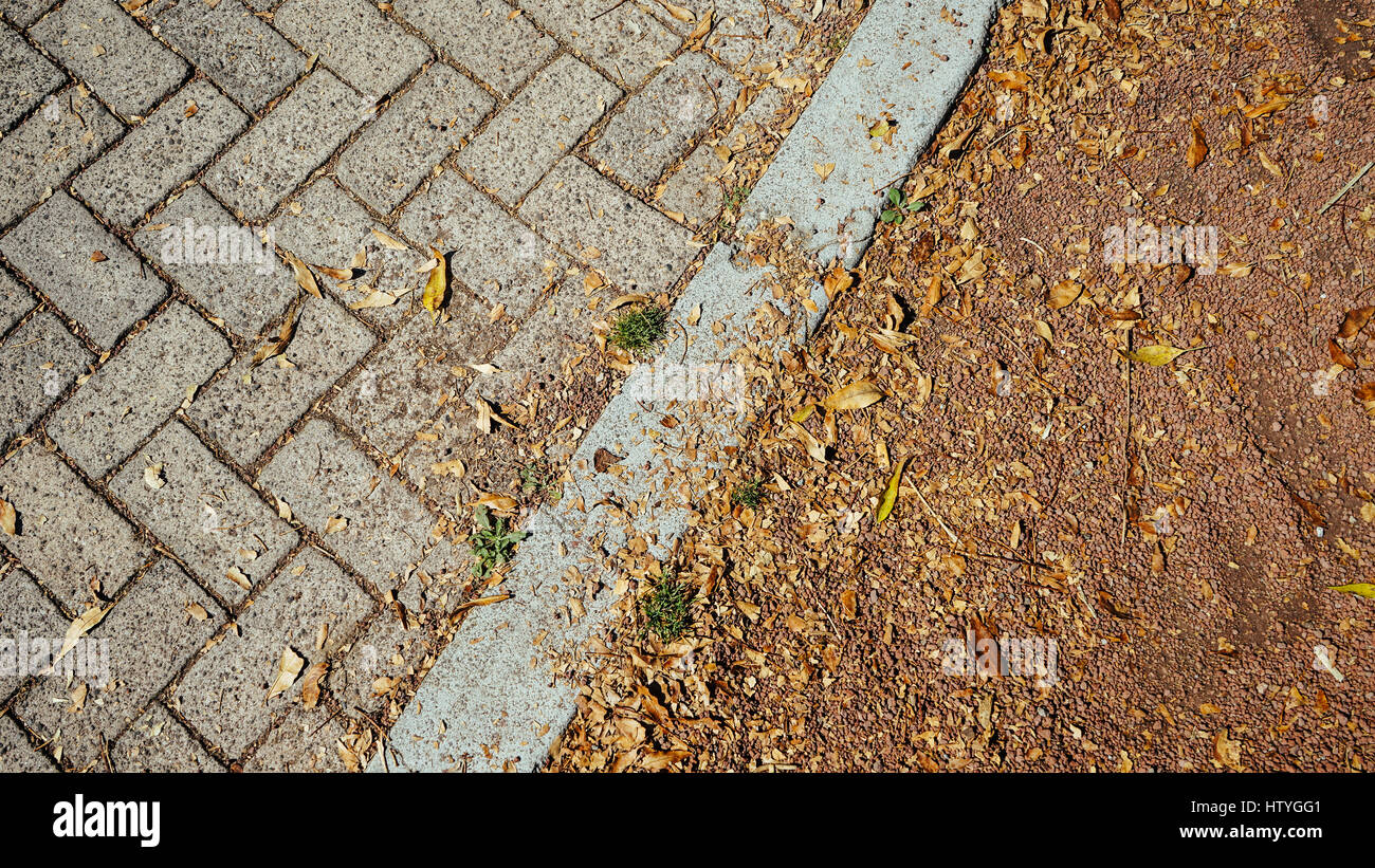 A grey brick ground split between dirt and leaves Stock Photo - Alamy