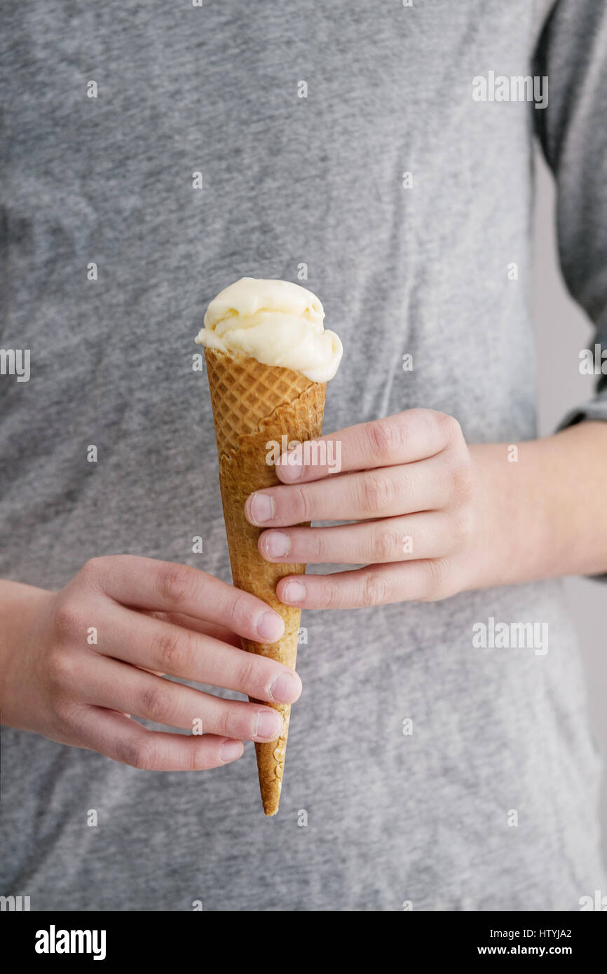 Vanilla soft elastic ice cream in waffle cone in boy hands. Boy in gray ...