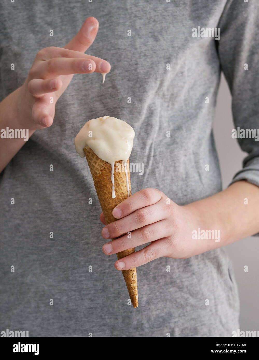 Vanilla soft elastic ice cream in waffle cone in boy hands. Boy in gray ...