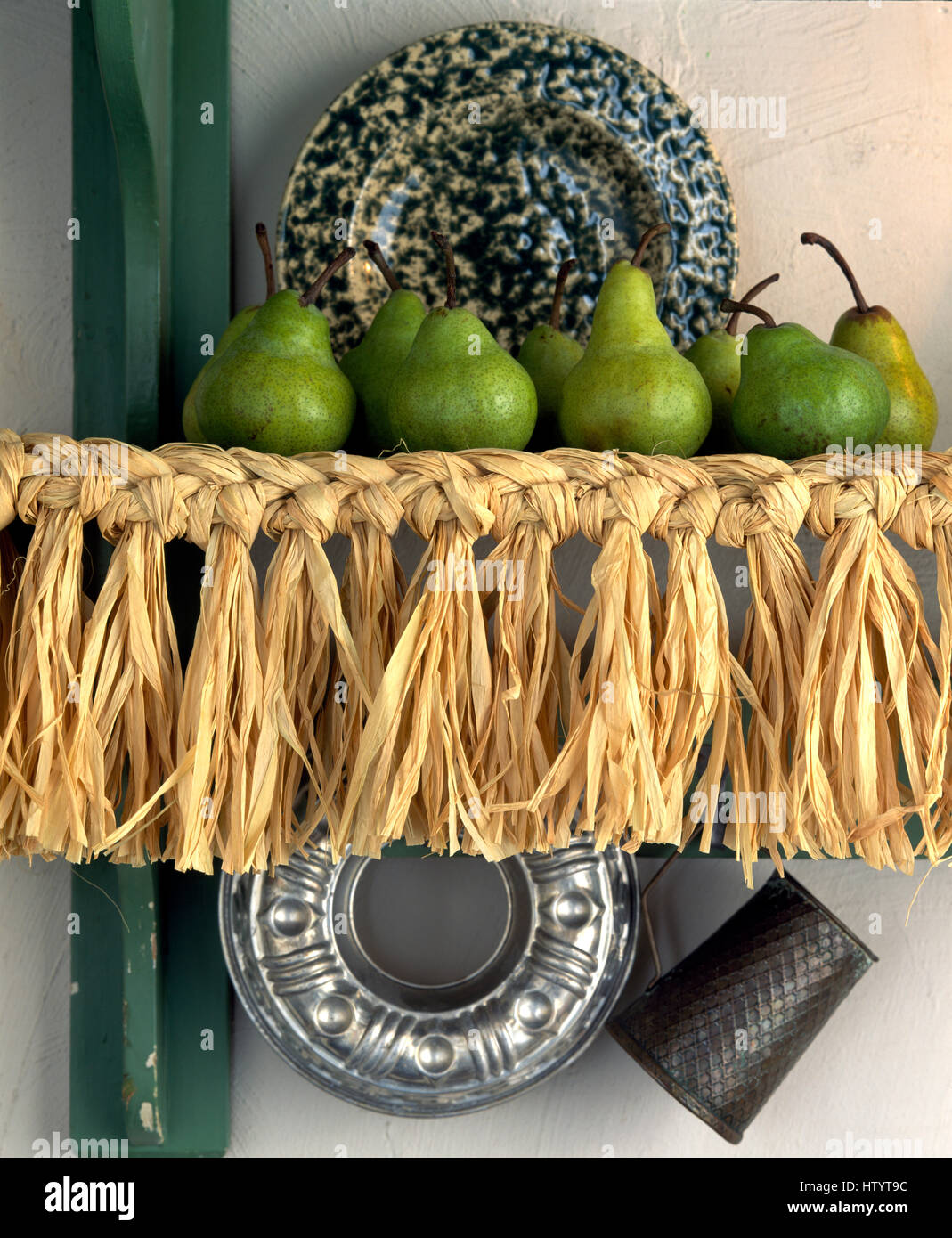 Close-up of green pears on a shelf with a plaited and tasseled raffia ...
