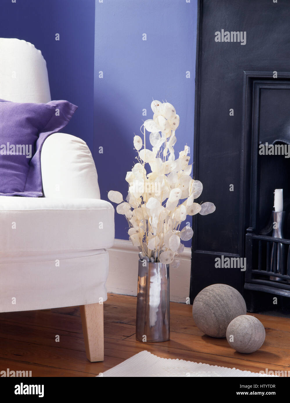 Dried honesty in a metal vase beside white armchair in a deep blue ...