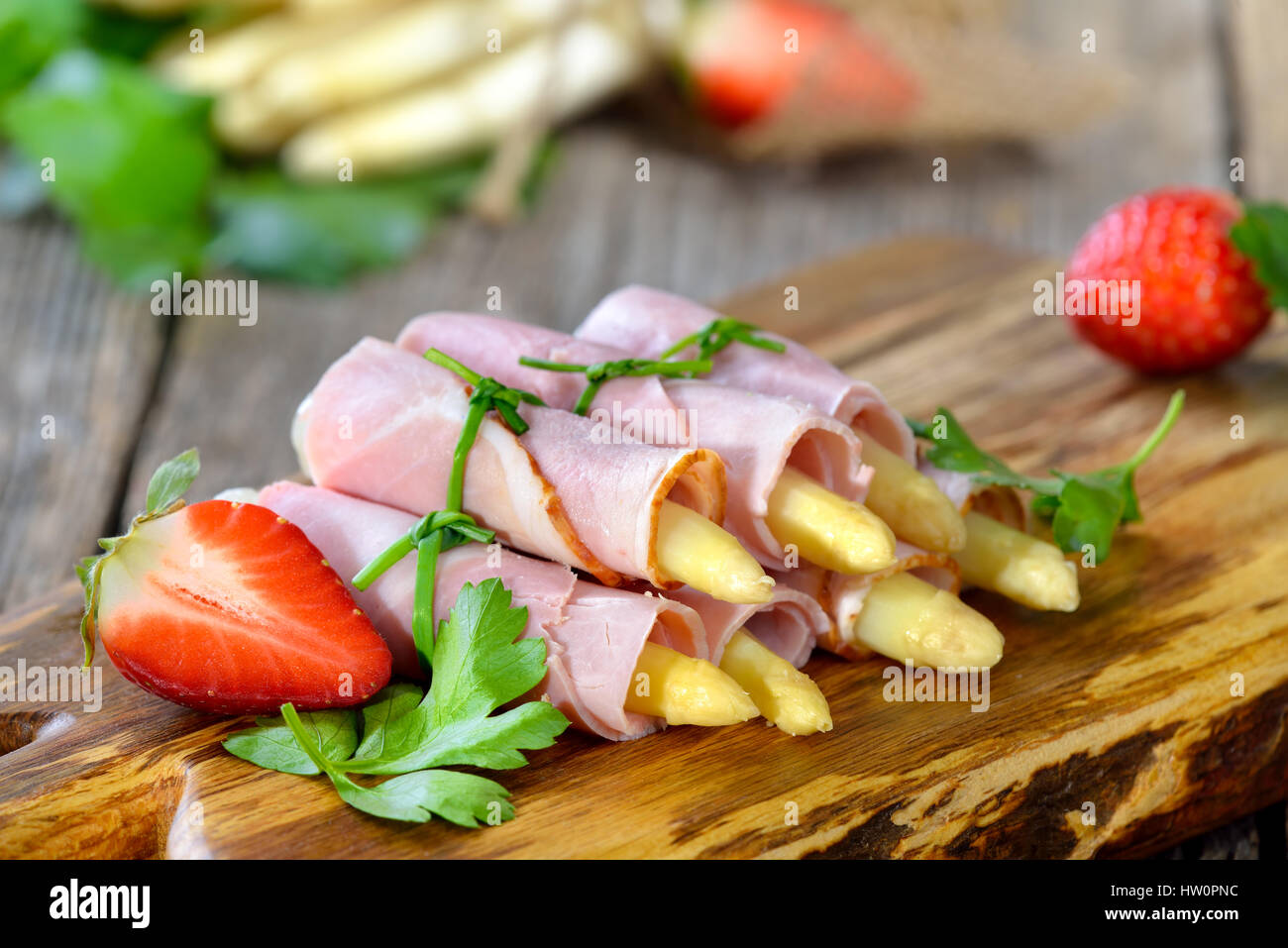 Rolls of cooked ham with fresh white asparagus tied with chives and ...