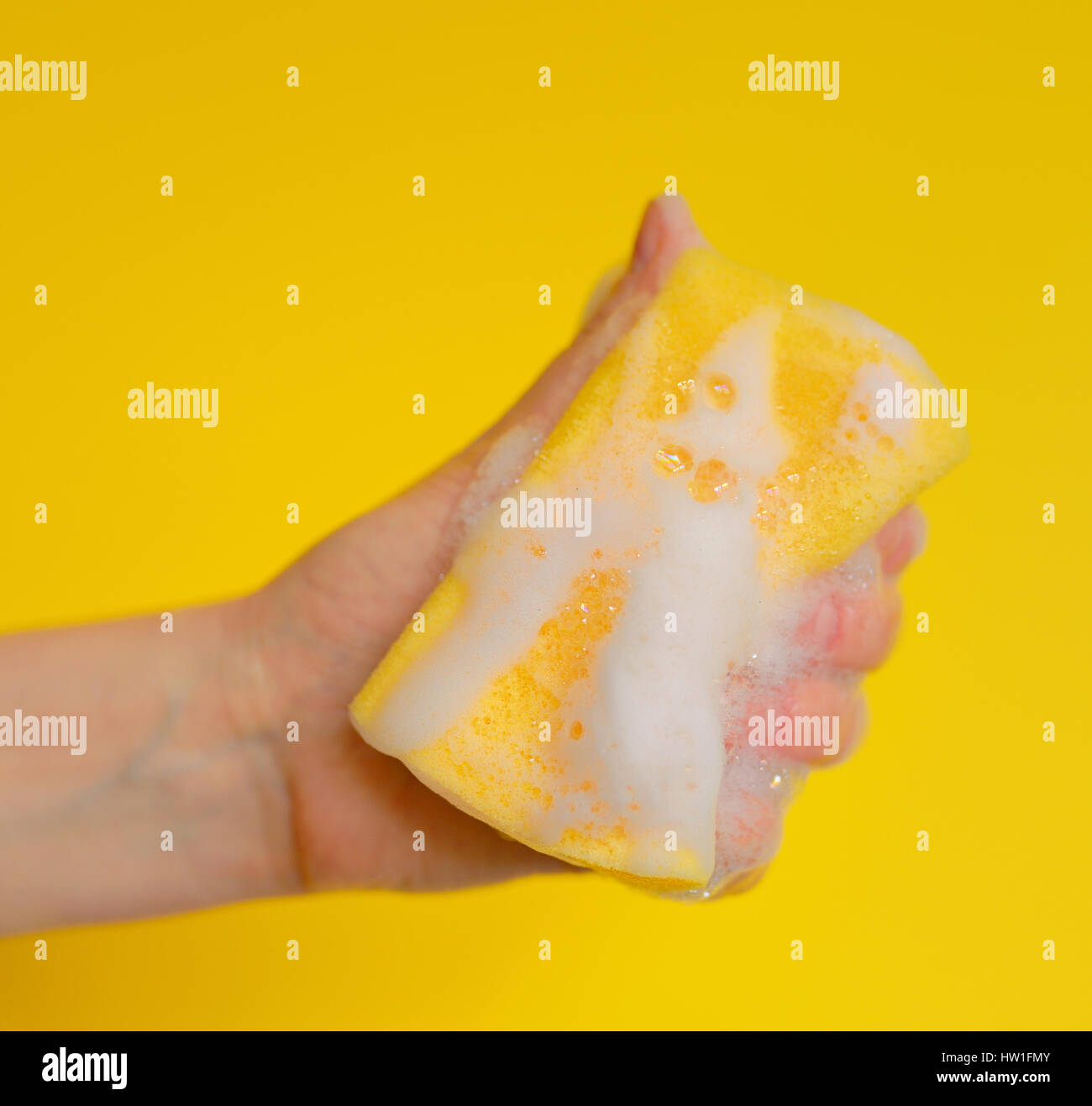 Hand with sponge with foam on yellow background Stock Photo - Alamy