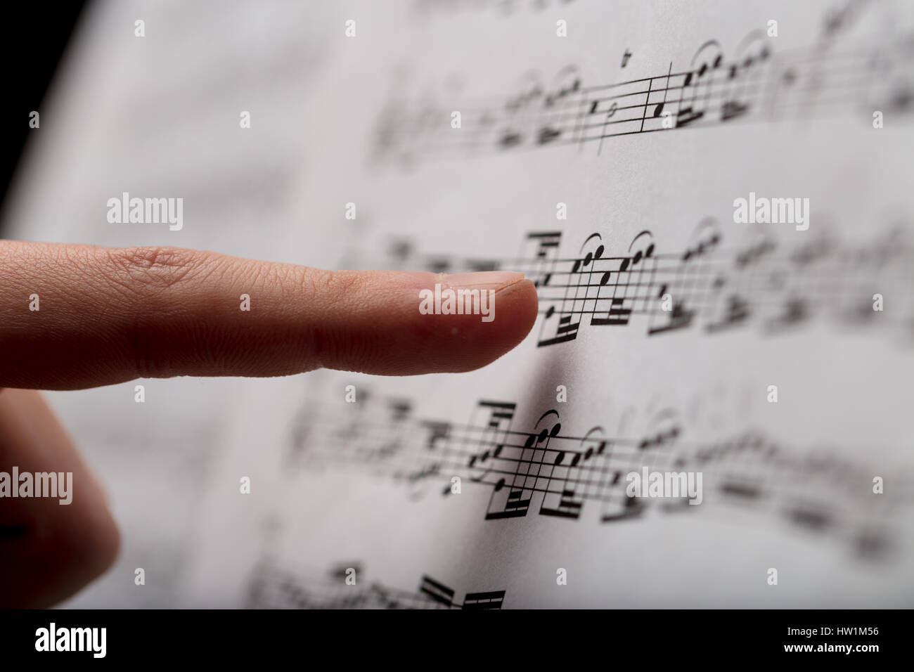 index finger on foreground pointing out some musical notes on a music ...