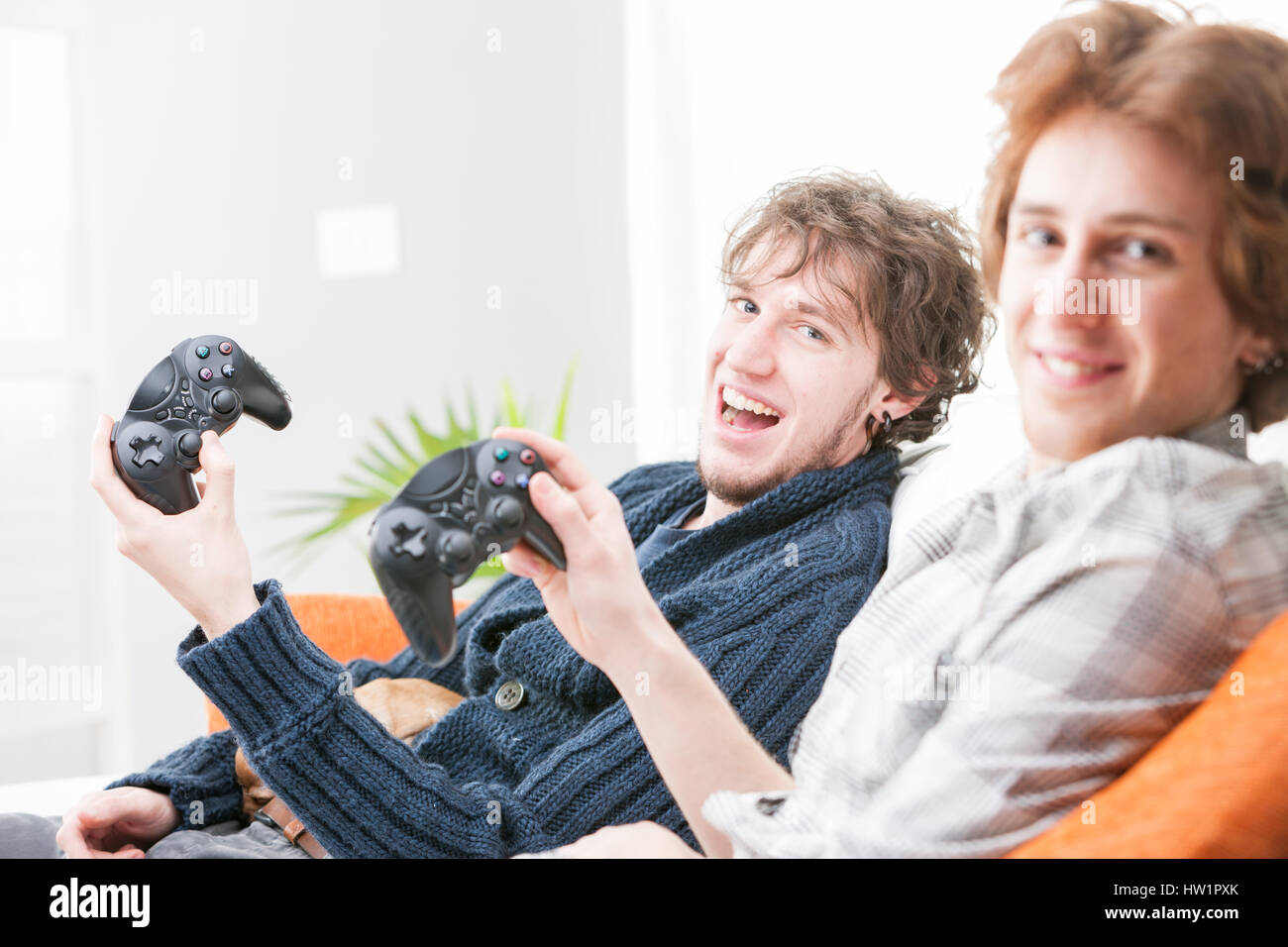 Two animated brothers playing video games together on a sofa at home ...