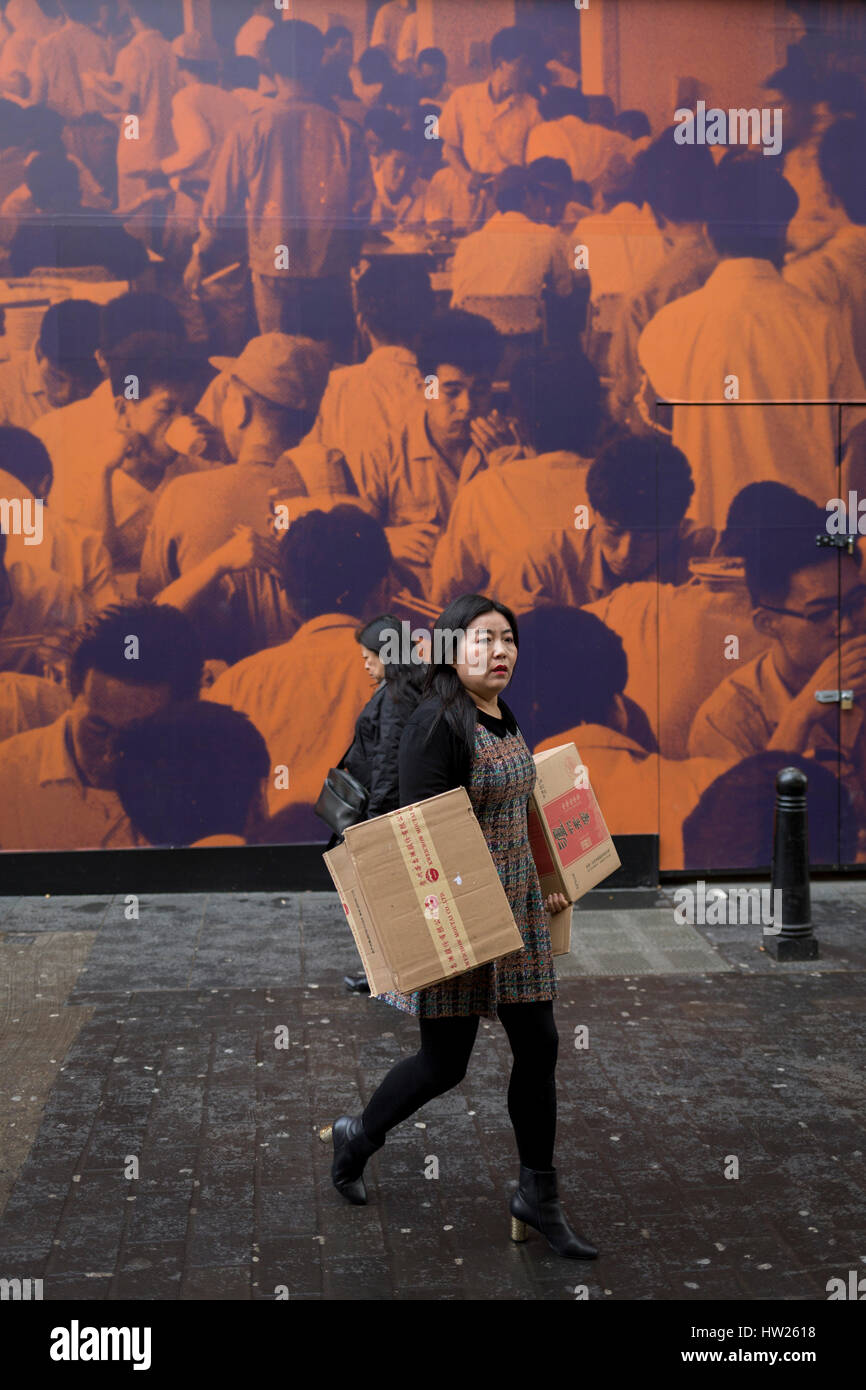 A Chinese lady carries boxes and walks in front of a construction ...