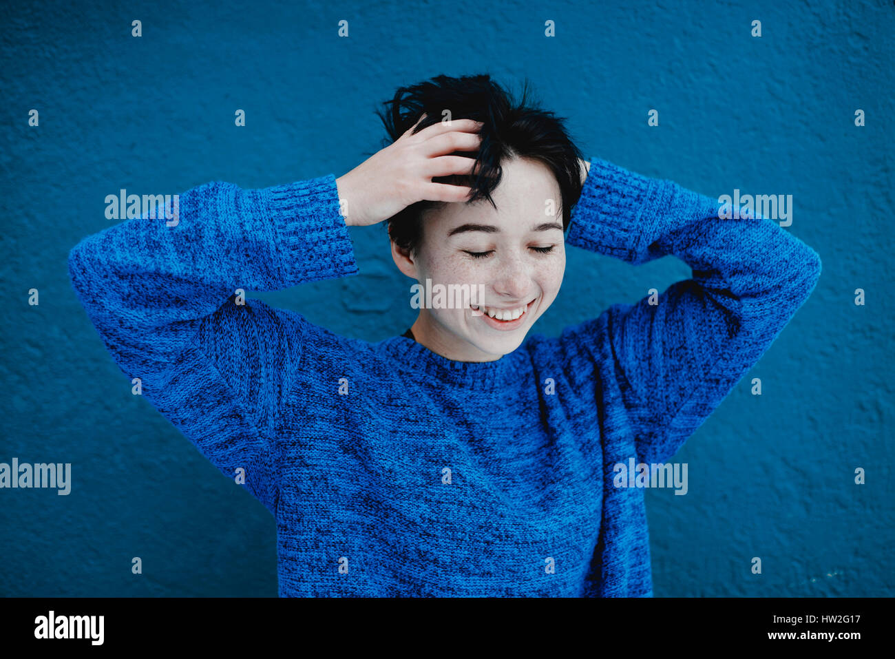 Smiling Caucasian woman tousling hair near blue wall Stock Photo - Alamy