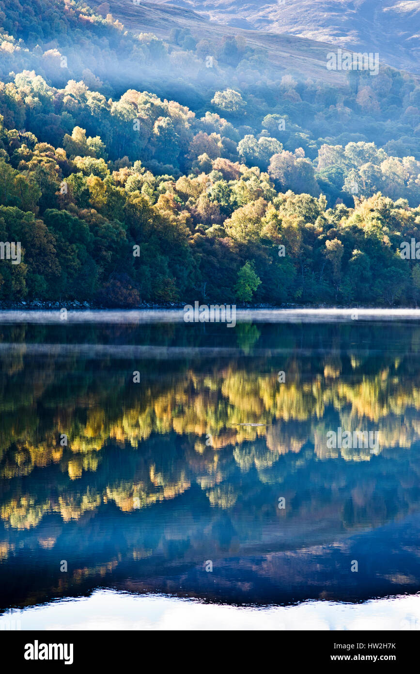 Colourful autumnal trees reflected in the calm water of Loch Rannoch ...