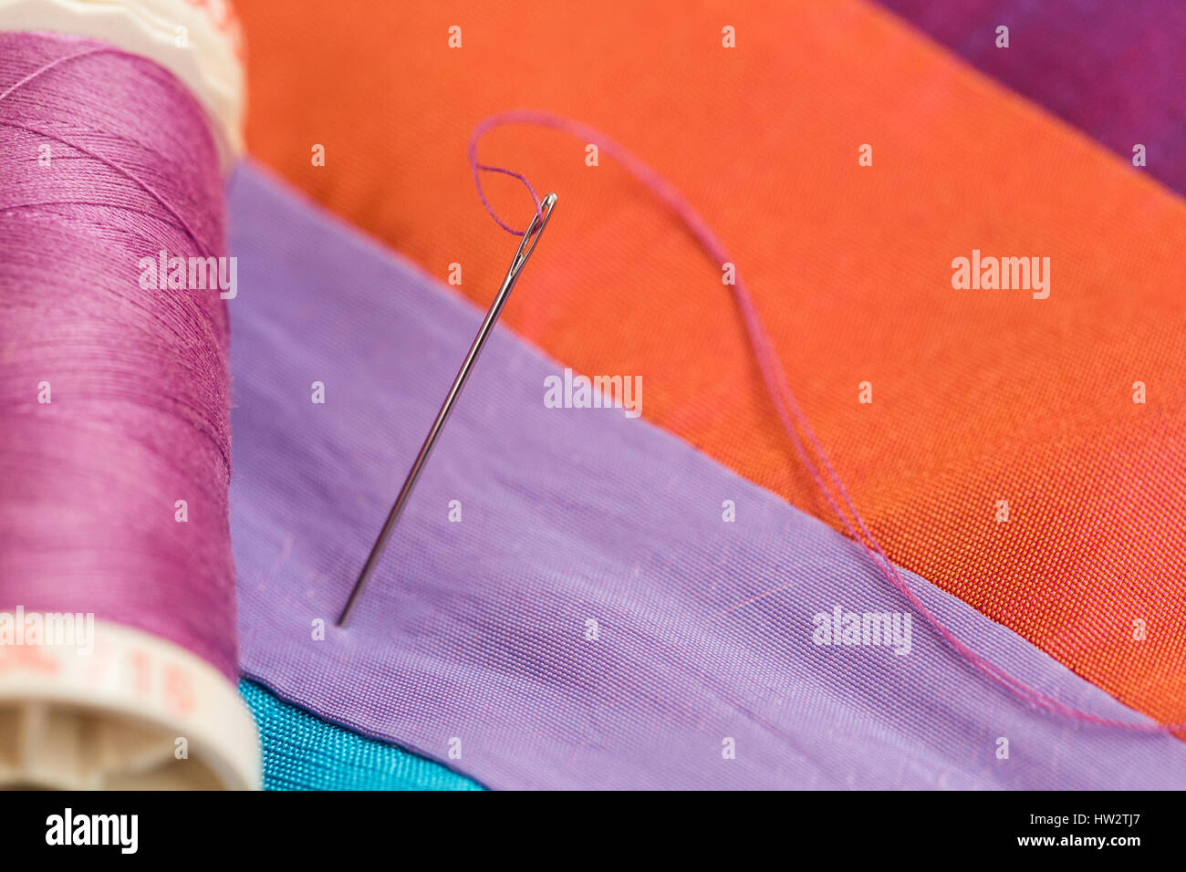 Thread passing through needle eye close-up on orange background. the ...