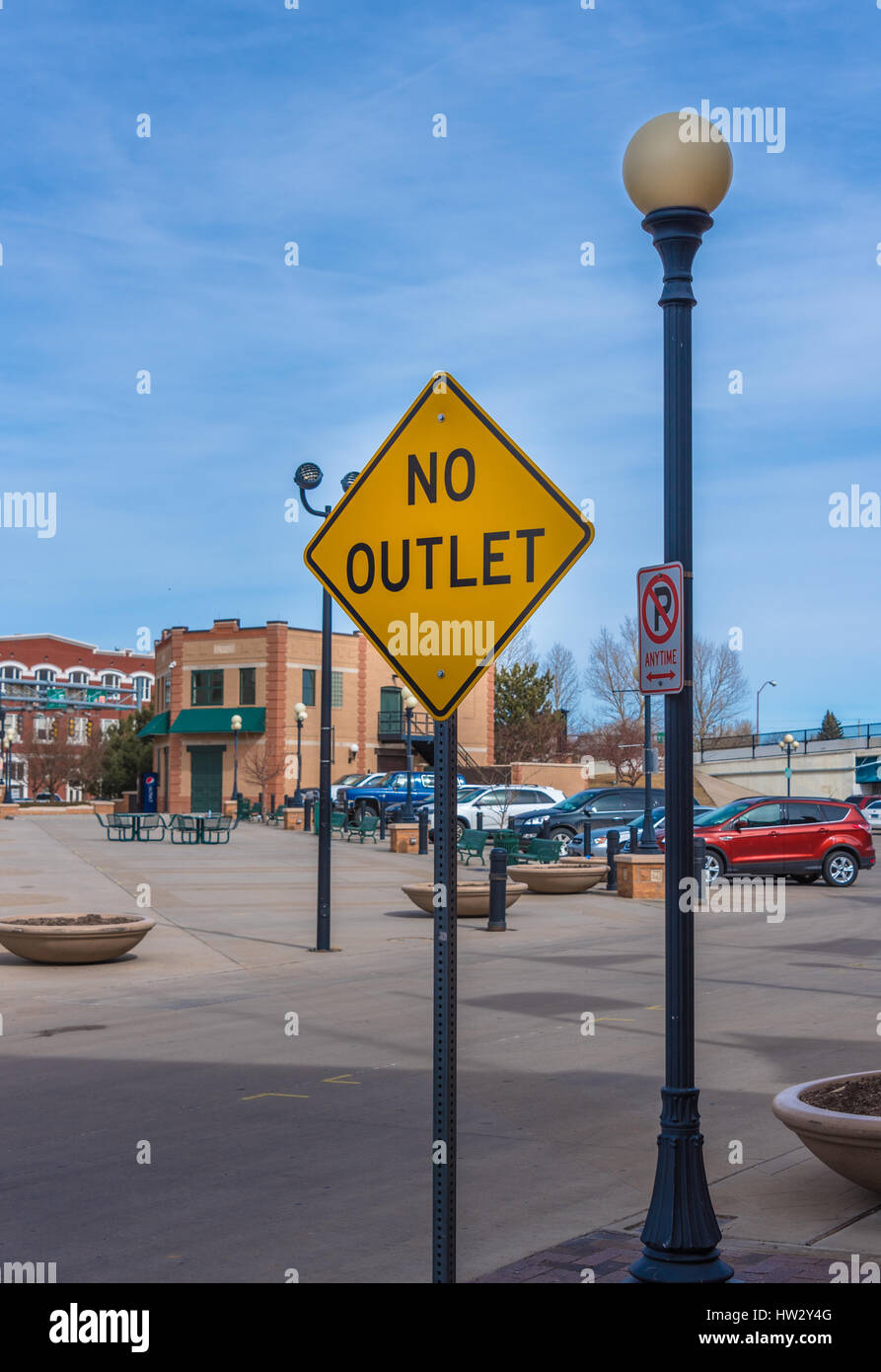 A yellow no outlet sign next to a light pole with a blue sky background ...