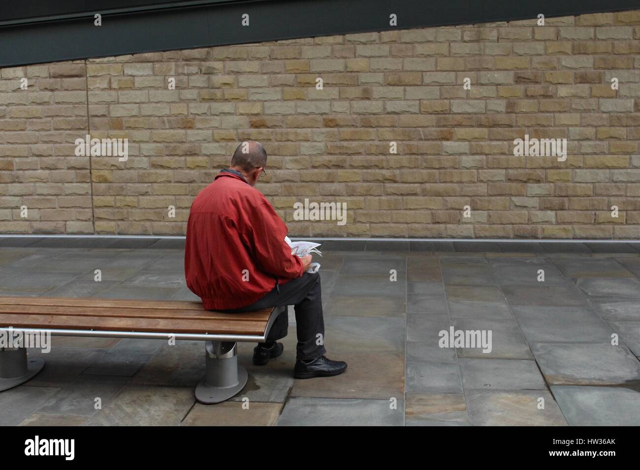 A man sits alone reading the newspaper on a bench Stock Photo - Alamy