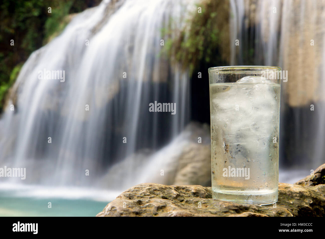 Dewy glass full of water with ice cube stands on a rock near a ...