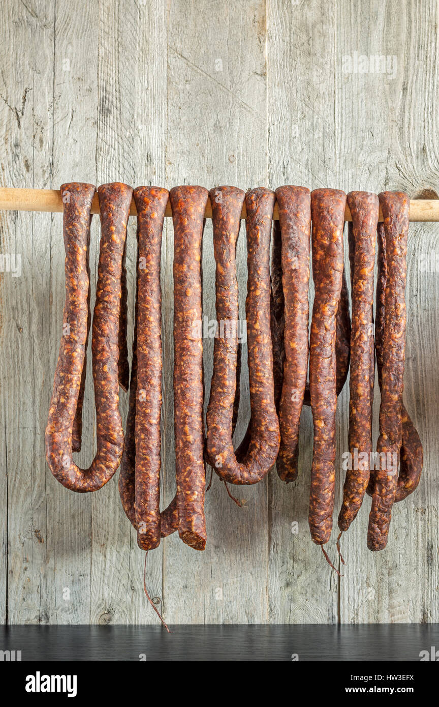 Row of smoked pork sausage in natural casings hanging on a wooden pole ...
