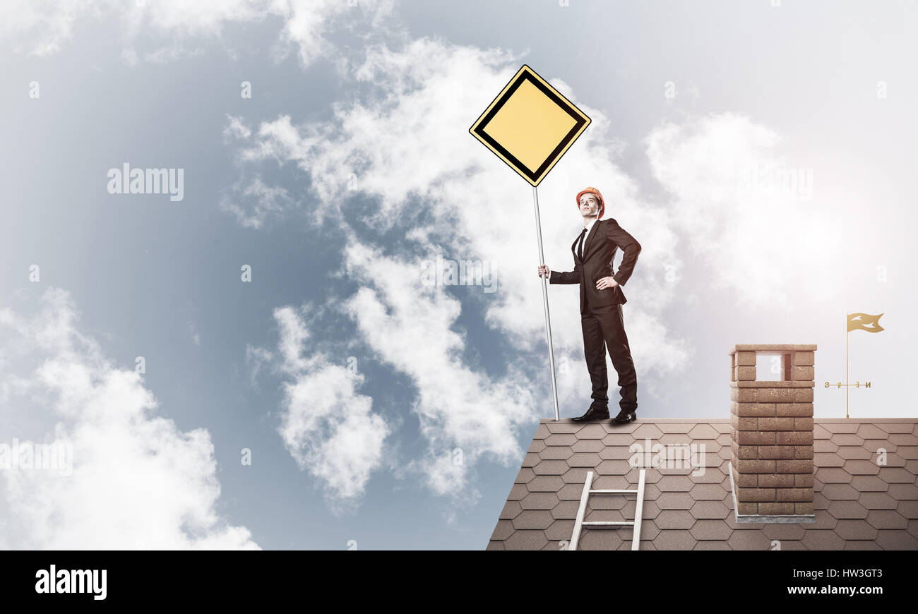Young businessman on house brick roof holding yellow signboard Stock ...