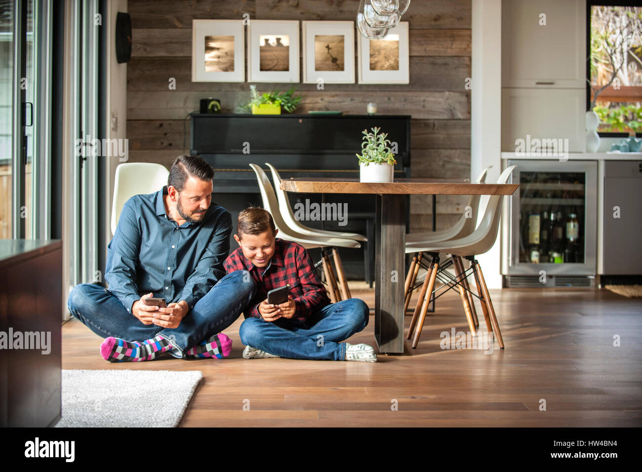 Smiling father and son sitting on floor texting on cell phones Stock ...