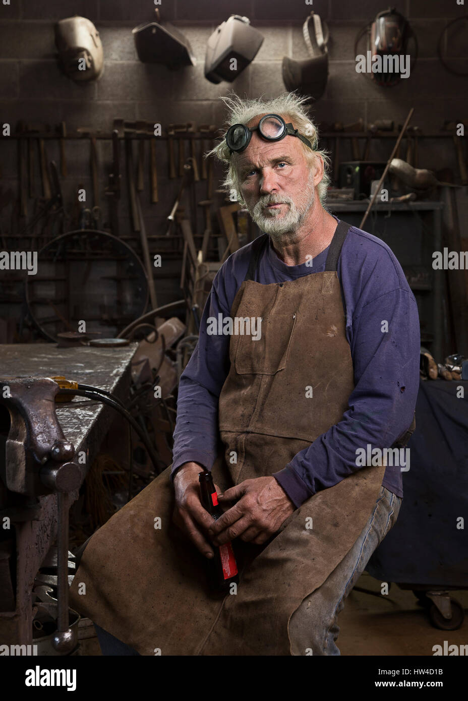 Portrait of serious Caucasian blacksmith in workshop drinking beer ...