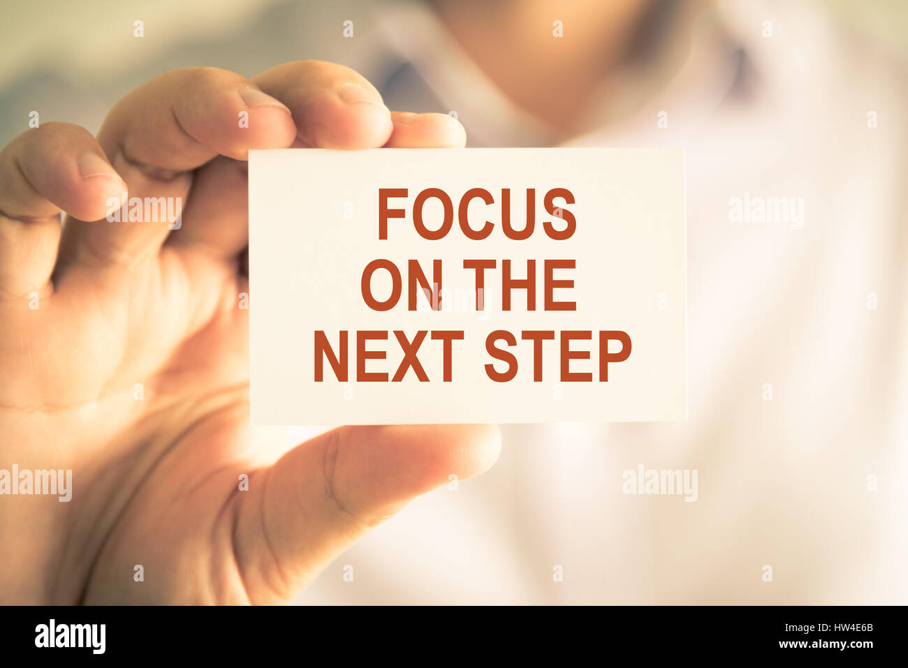 Closeup on businessman holding a card with text FOCUS ON THE NEXT STEP ...