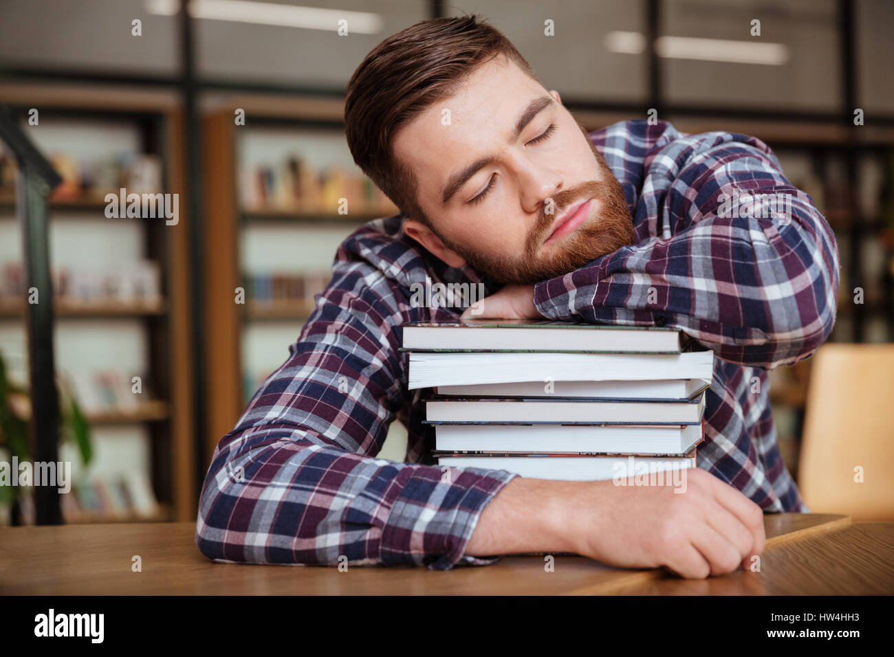 Young tired male student taking a nap on a stack of books in library ...