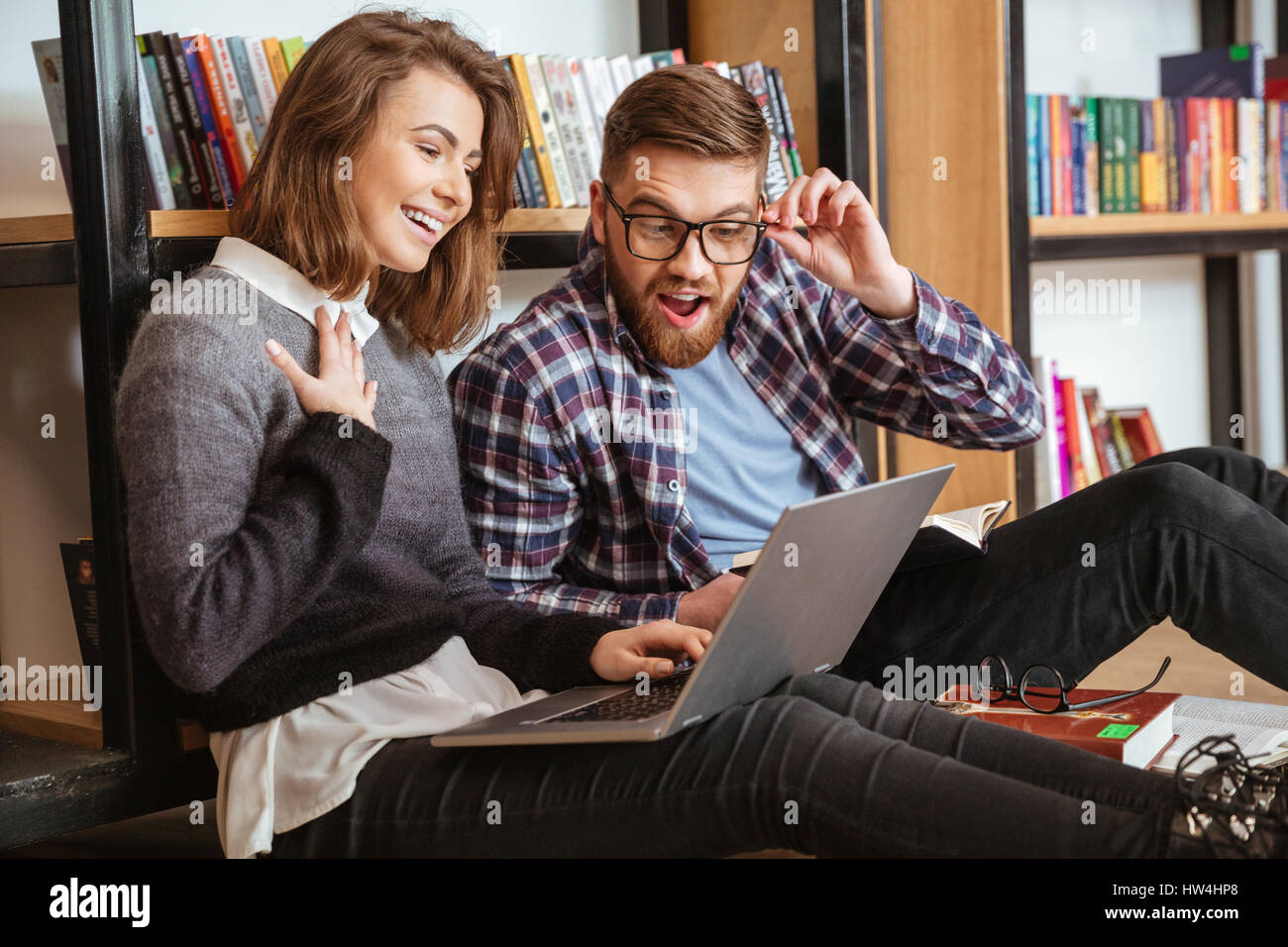 Happy students with laptop computer networking in library while sitting ...