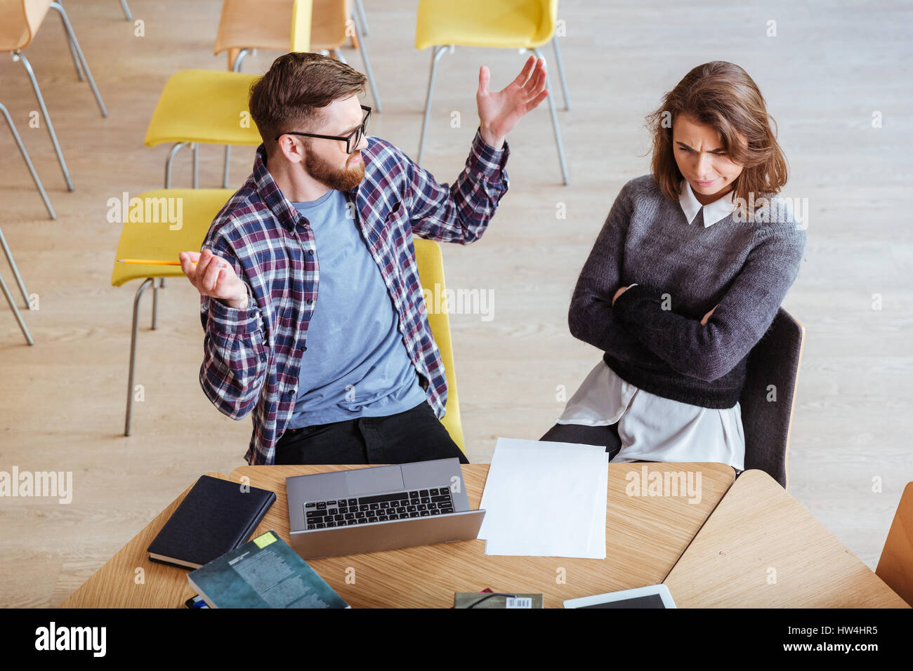 Photo of young angry students sitting in library while writing notes ...