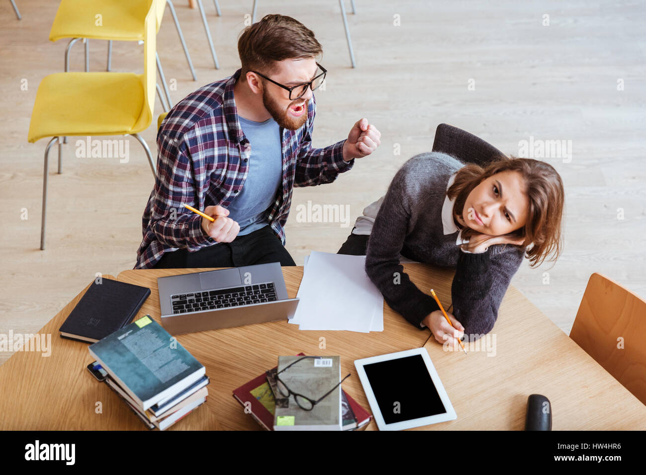 Image of two angry students sitting in library while writing notes and ...
