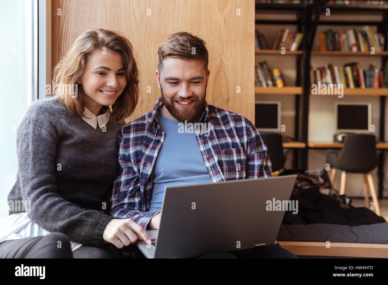 Happy students with laptop computer networking in library while sitting ...