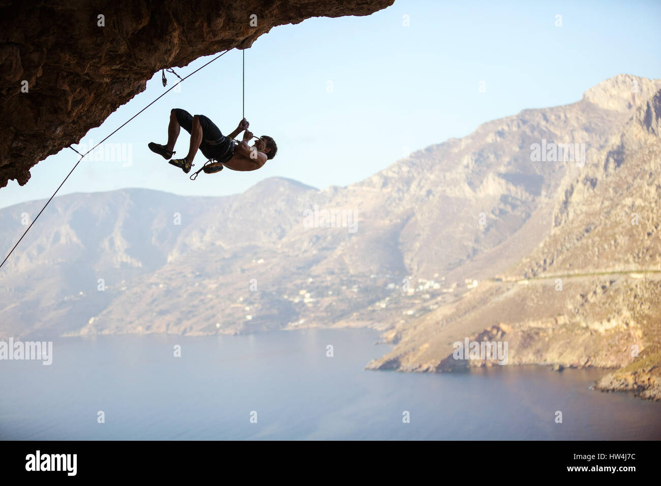 Young man trying to reach cliff in order to continue climbing ...
