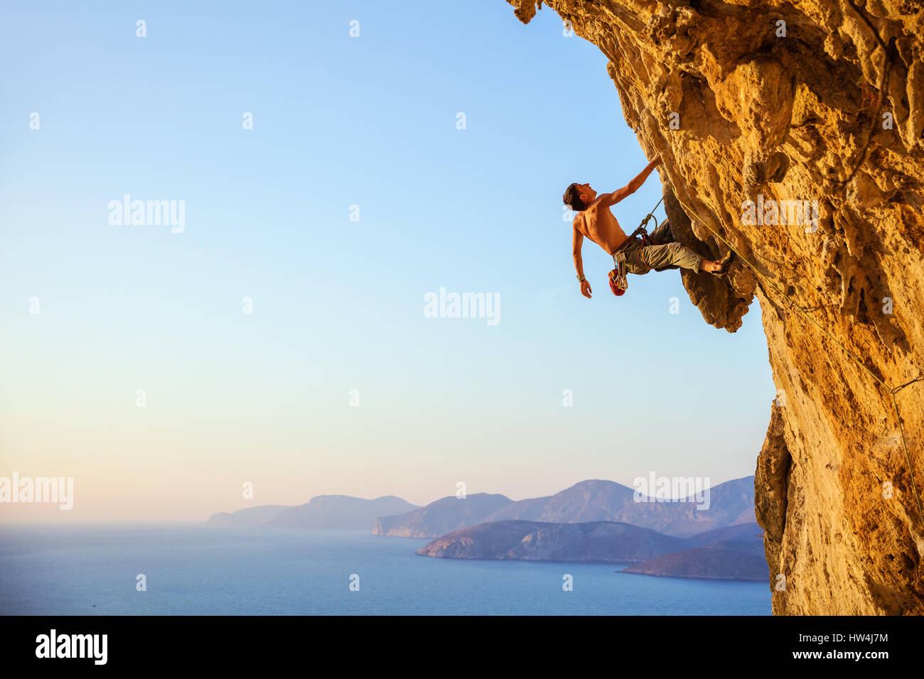 Young man looking up while climbing challenging route on cliff, view of ...