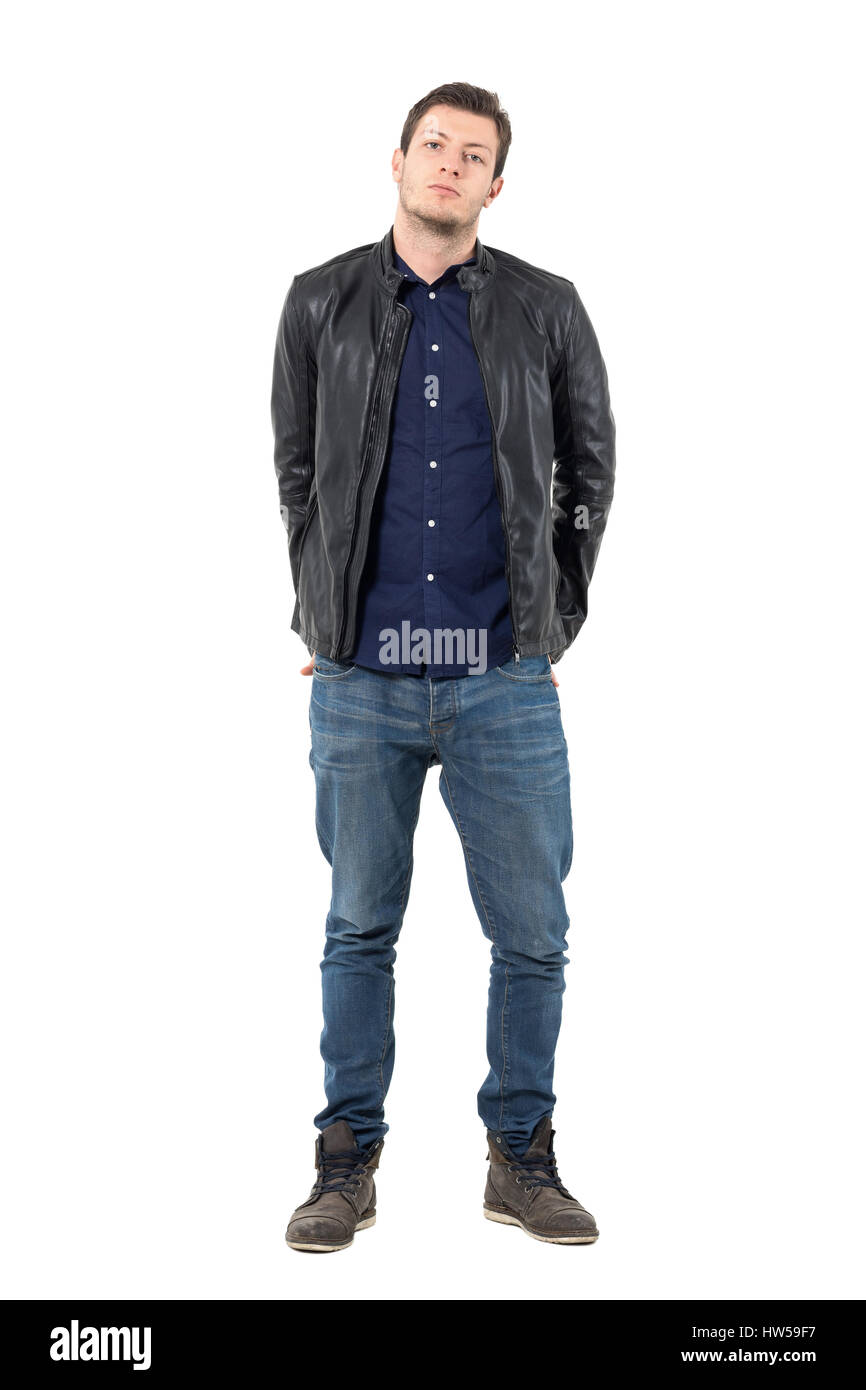 Young man in leather jacket and jeans with hands behind back and titled ...